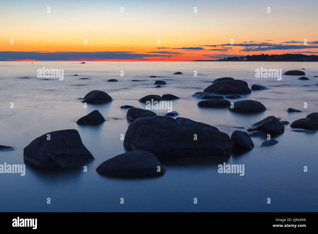 Rocky shore with stones sinking in the sea water. Sunset, long exposure ...