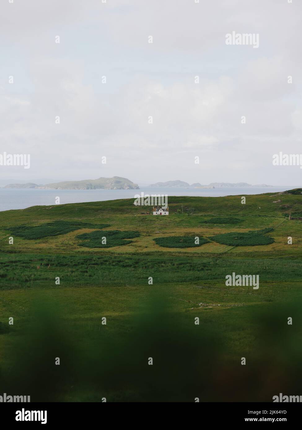 The summer green landscape and a lone white croft in Polglass Loch ...