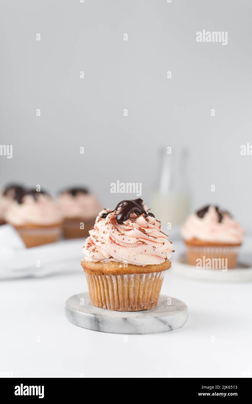 Vanilla cupcake with a tall swirl of pink frosting, chocolate glaze and ...