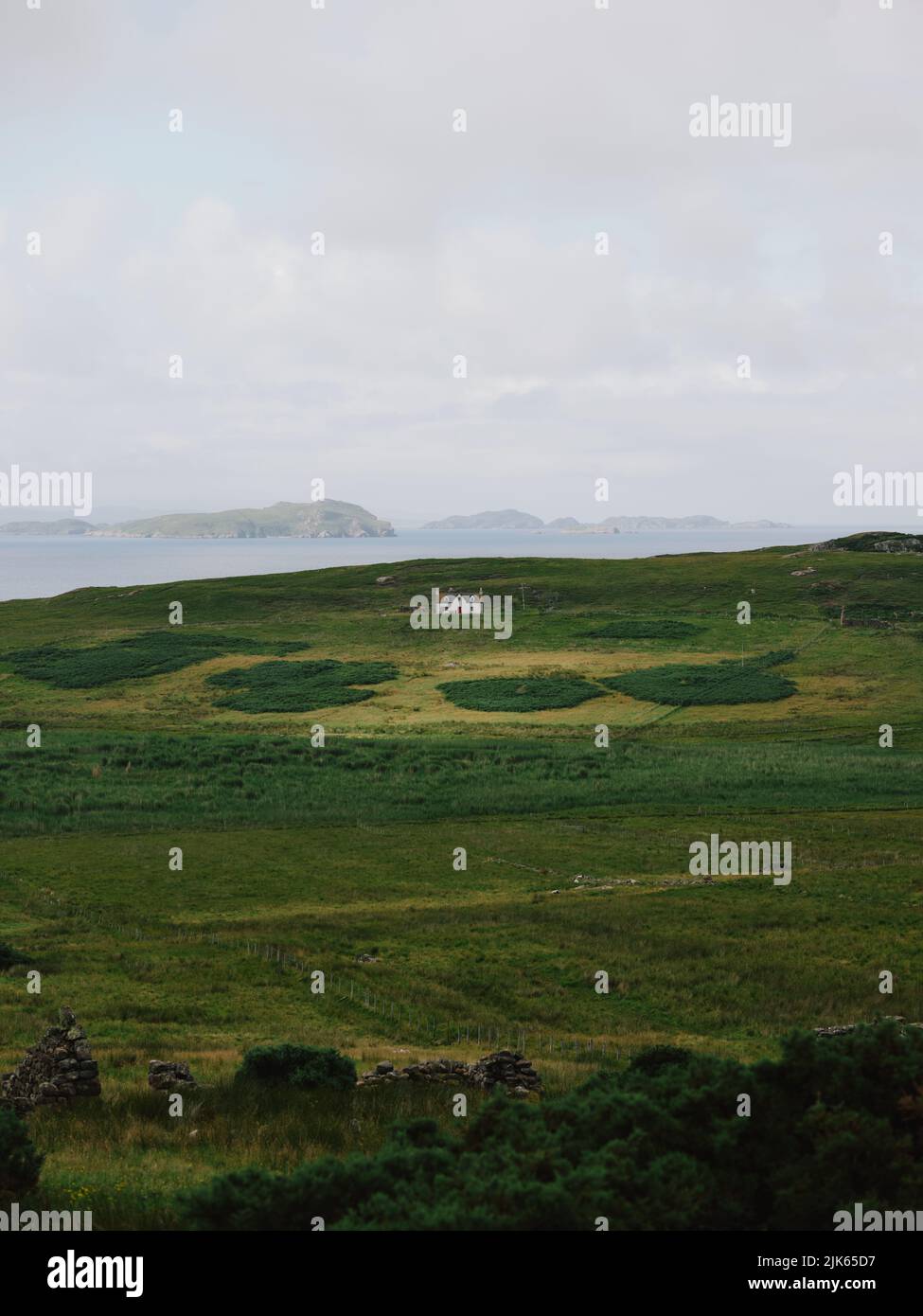The summer green landscape and a lone white croft in Polglass Loch ...