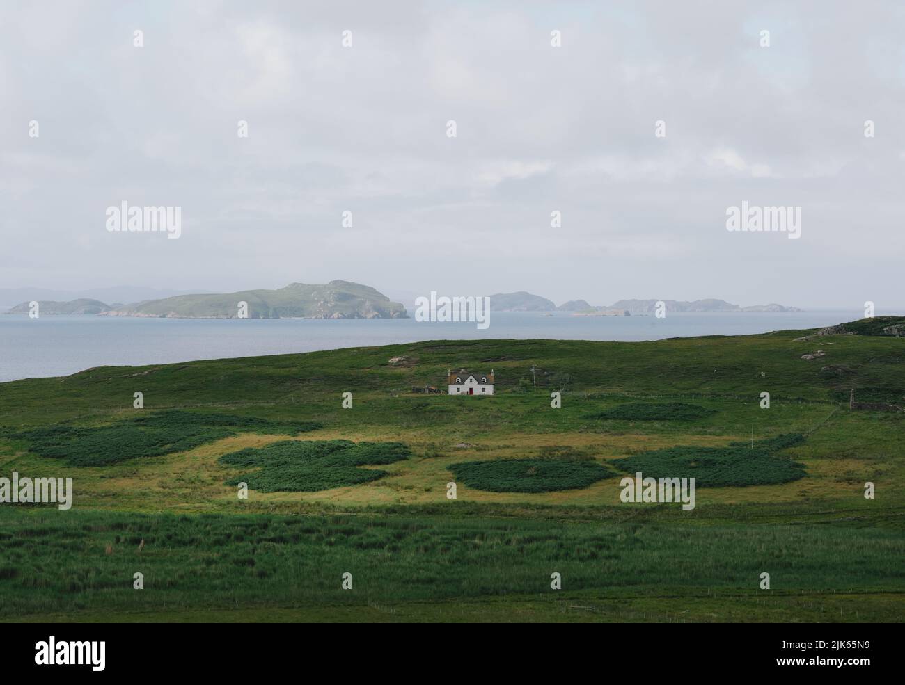 The summer green landscape and a lone white croft in Polglass Loch ...