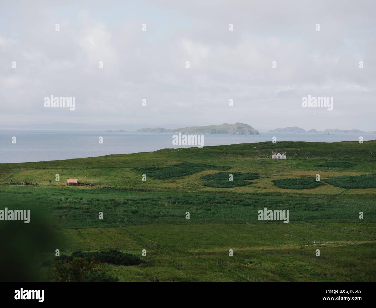 The summer green landscape and a lone white croft in Polglass Loch ...