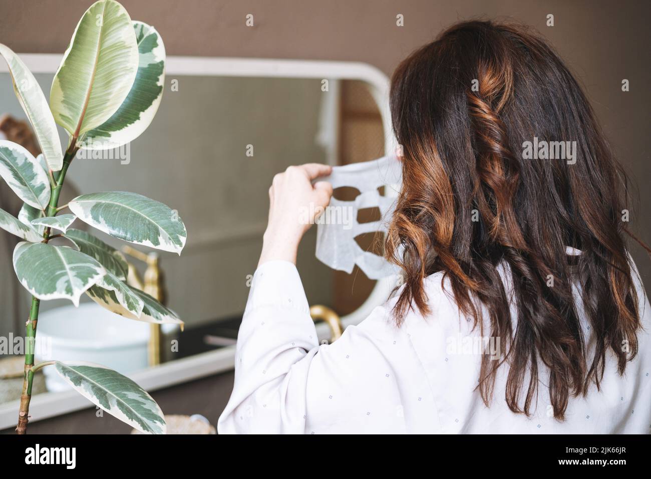 Adult brunette woman with sheet mask on her face in the bathroom at ...