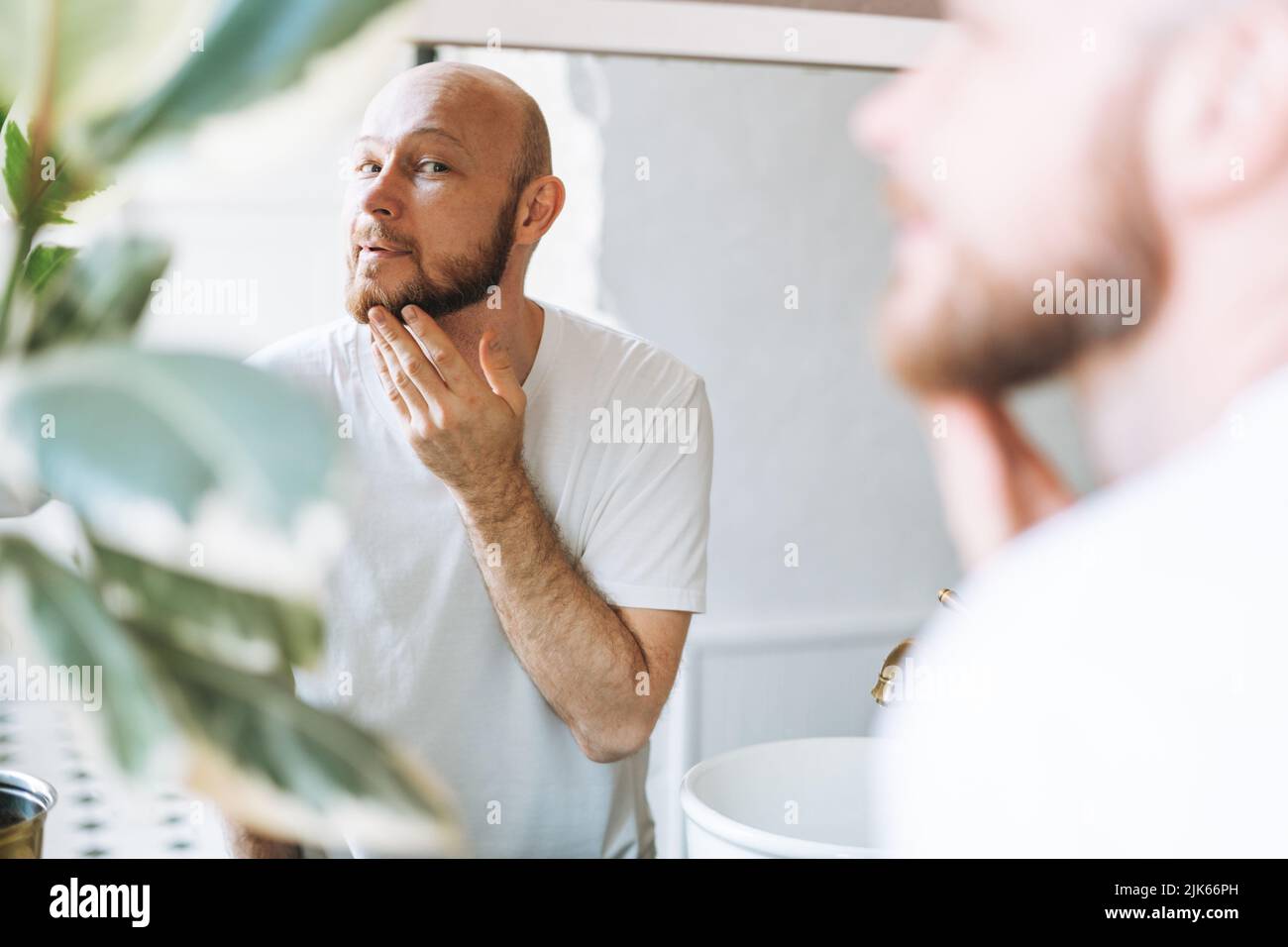 Handsome bald man looking at mirror and touching face in bathroom Stock ...