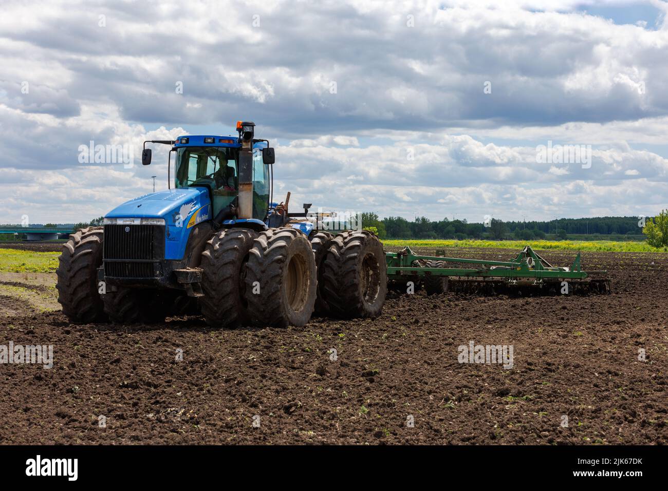 Blue tractor with double wheels pulling disc harrow with roller basket ...