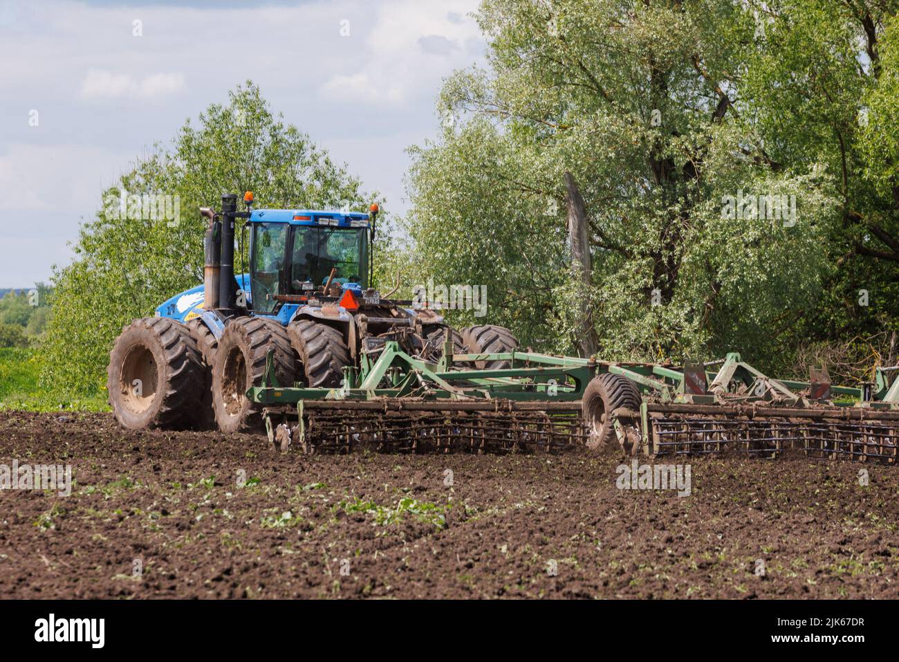 Blue tractor with double wheels pulling disc harrow with roller basket ...