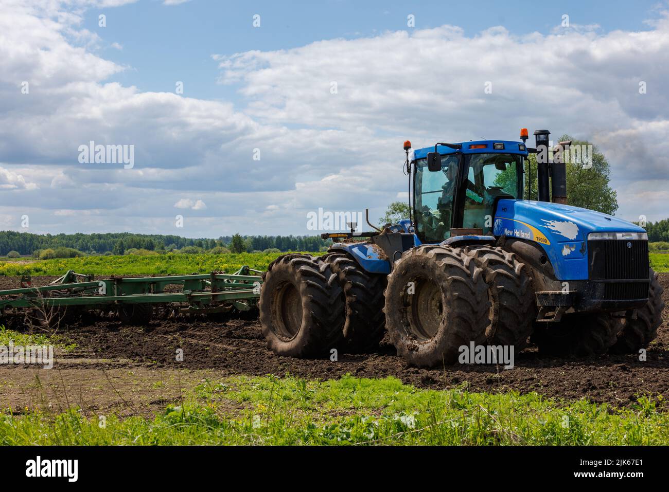 Blue tractor with double wheels pulling disc harrow with roller basket ...