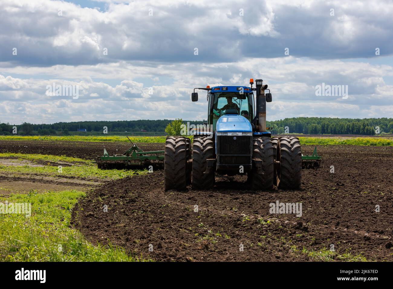 Blue tractor with double wheels pulling disc harrow with roller basket ...