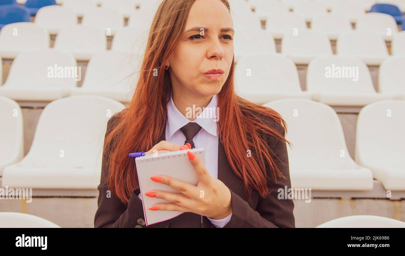 Young woman with notepad, pen sitting on stadium bleachers alone ...