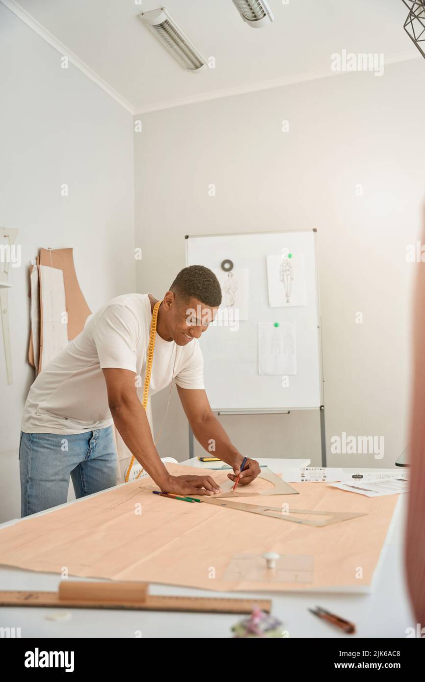 Jolly male tailor making dress patterns at desk Stock Photo - Alamy