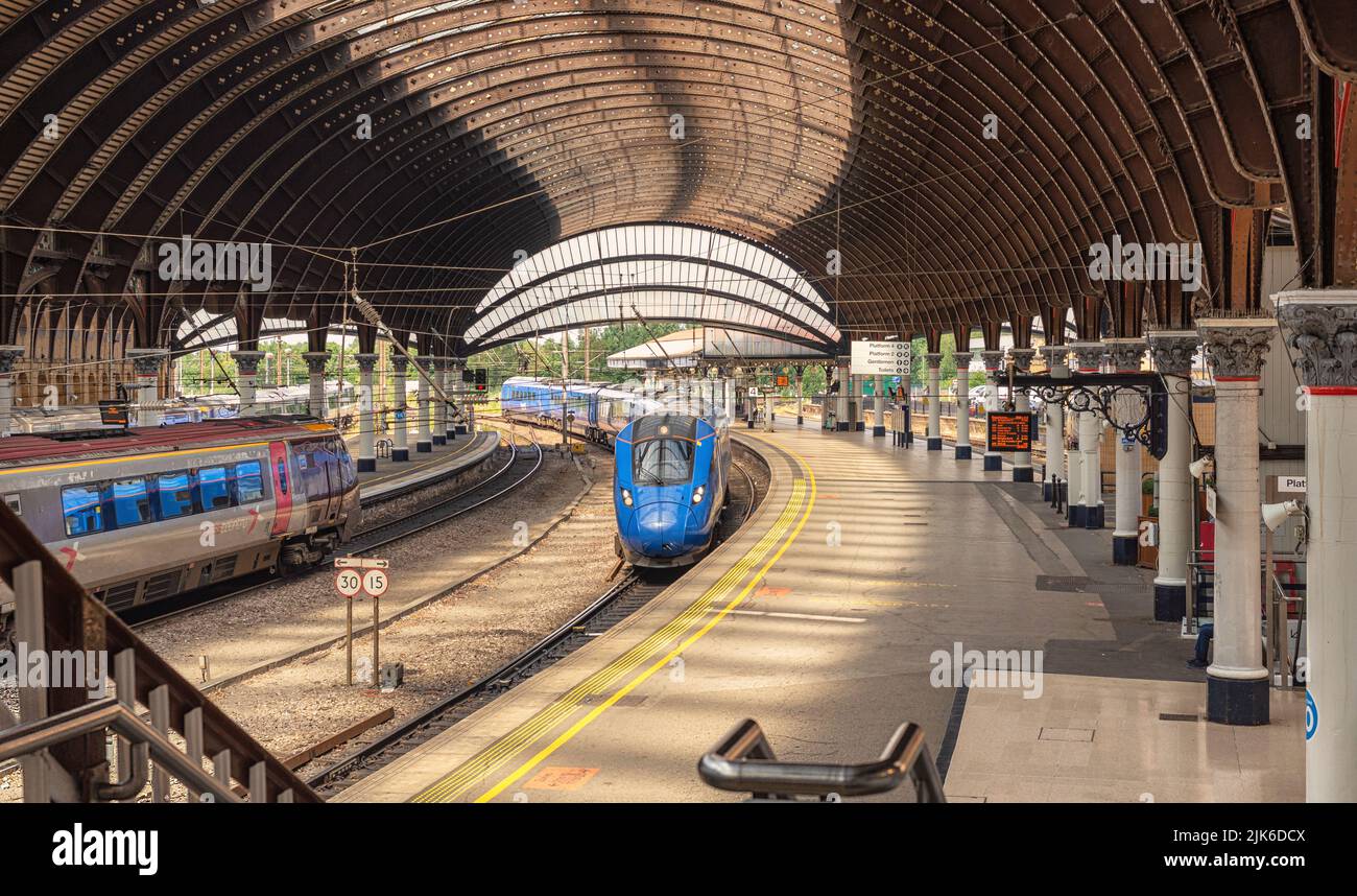 A modern train arrives at a railway station platform. A historic metal ...