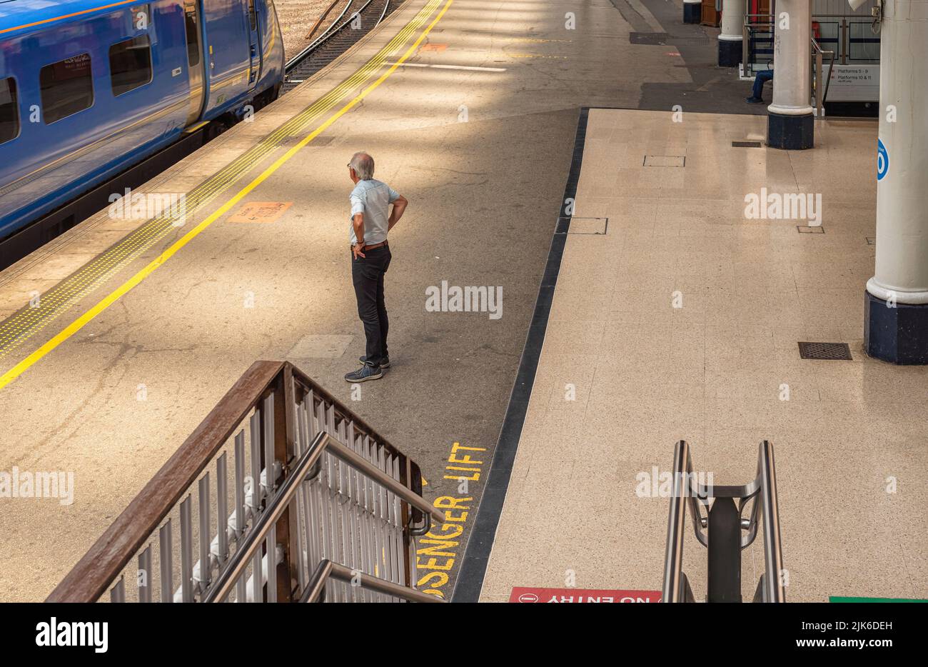 A man stands on a railway station platform watching a train speed by ...