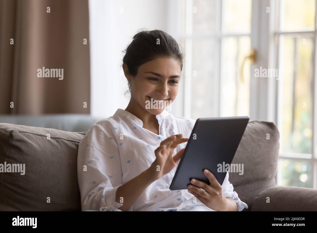 Happy young Indian tablet user woman resting on couch Stock Photo - Alamy