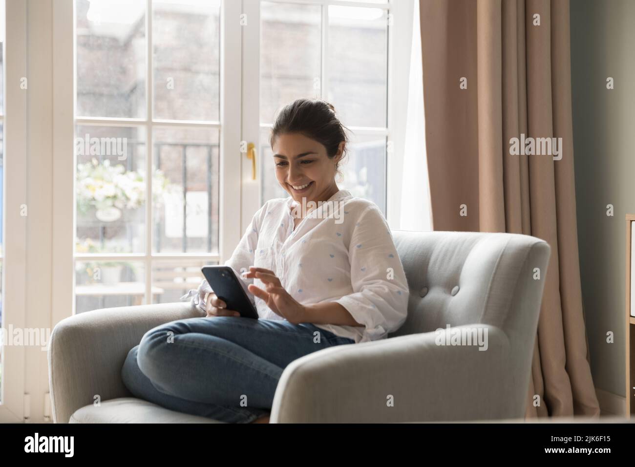 Cheerful beautiful Indian mobile phone user woman browsing Internet ...
