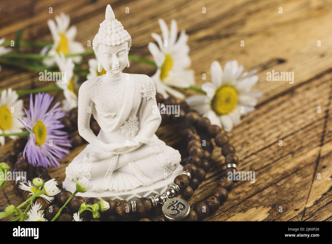 Buddha statue, prayer beads with OM symbol and wild flowers on a wooden ...
