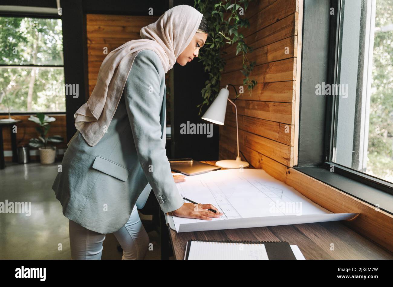 Pensive Muslim architect working with blueprints in a modern office. Creative young ...