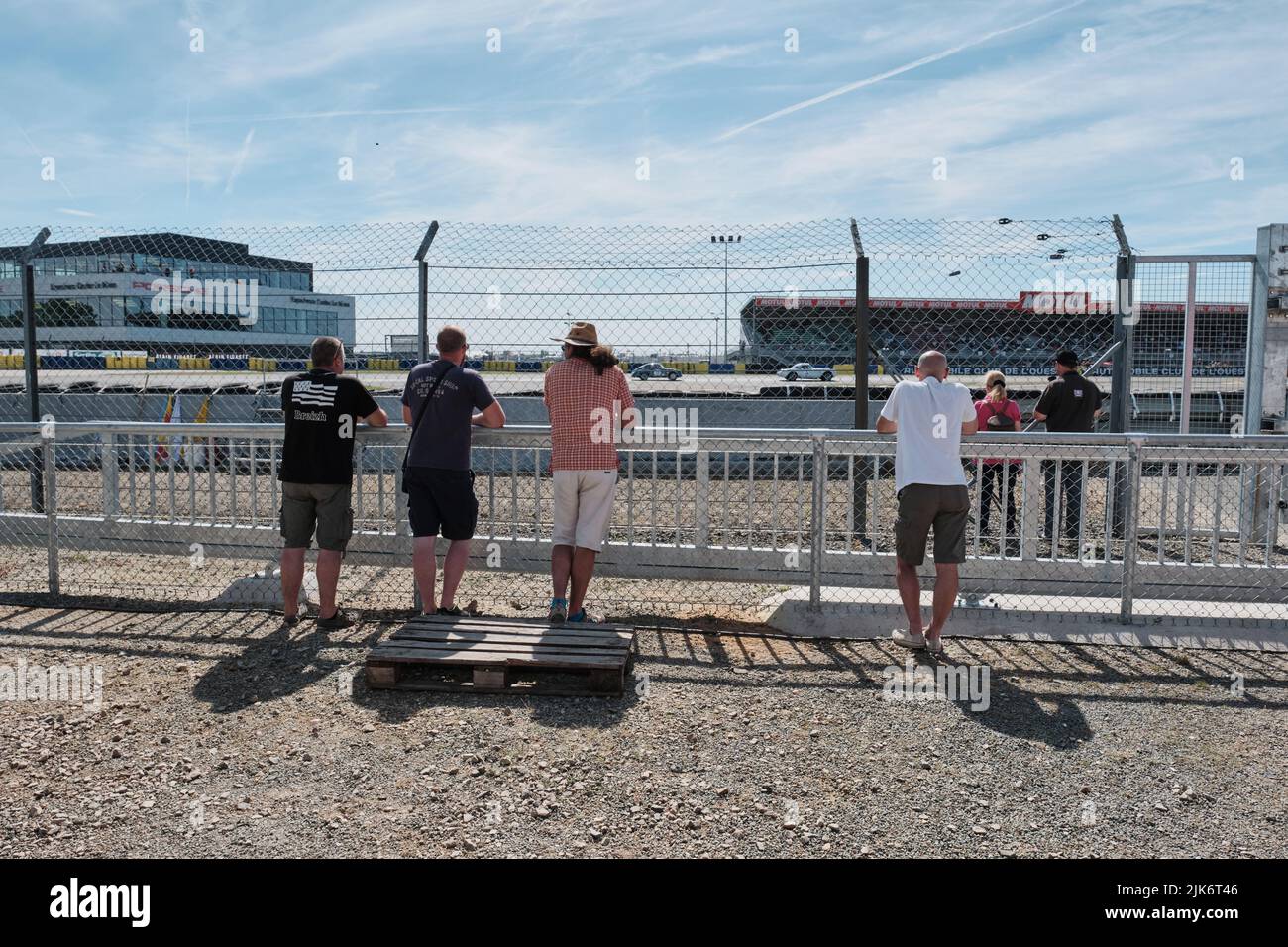 A group of people standing along the race track watching race cars ...
