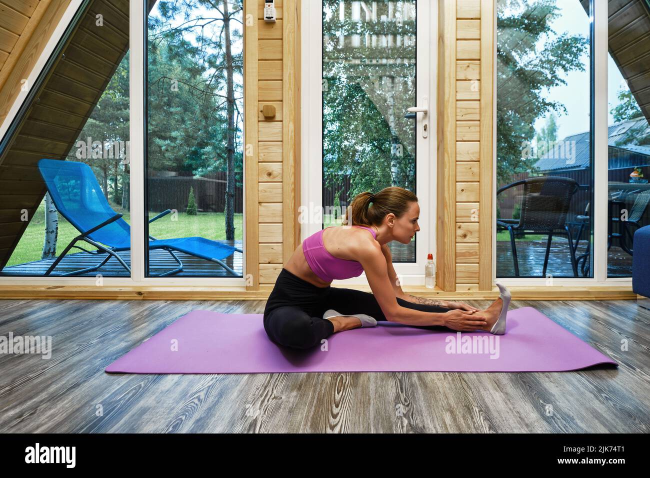 Active woman does stretching exercise at forest cabin during the rain ...