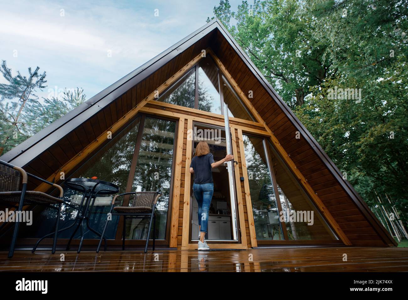 Back view of a woman opening the door of a forest chalet and enters ...