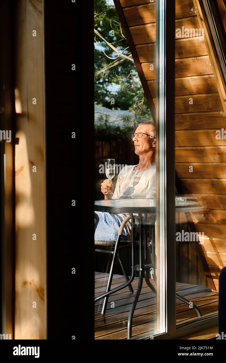 Man sits on terrace in sunny day with a glass of wine (view through the ...
