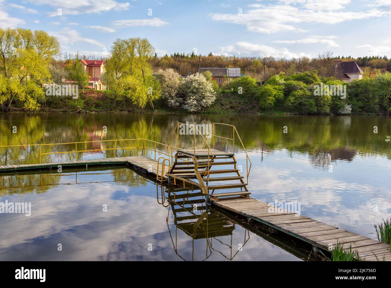 Beautiful spring landscape with calm river, wooden bridge, blooming ...