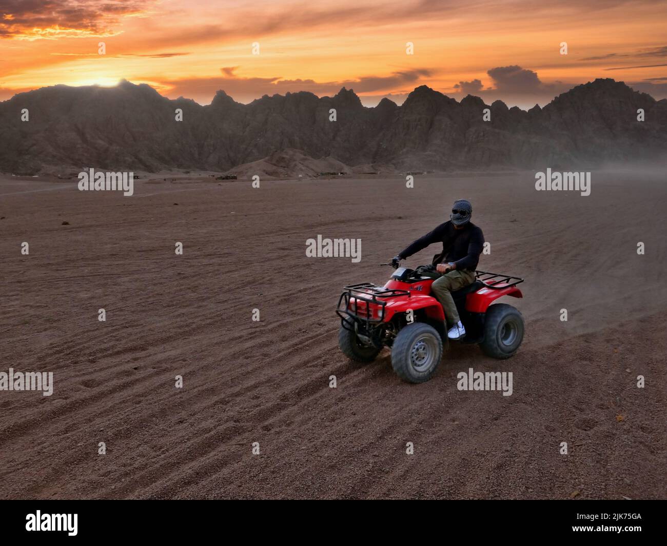 An unrecognizable man on a red quad bike in the Egyptian desert of ...