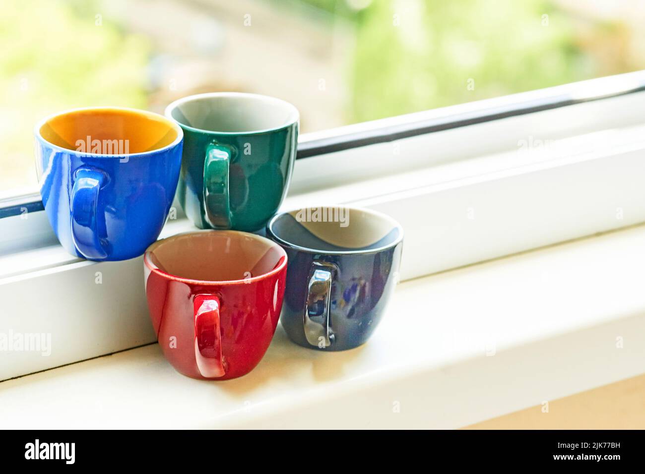 Four multi colored ceramic cups on the windowsill.Coffee and tea ...