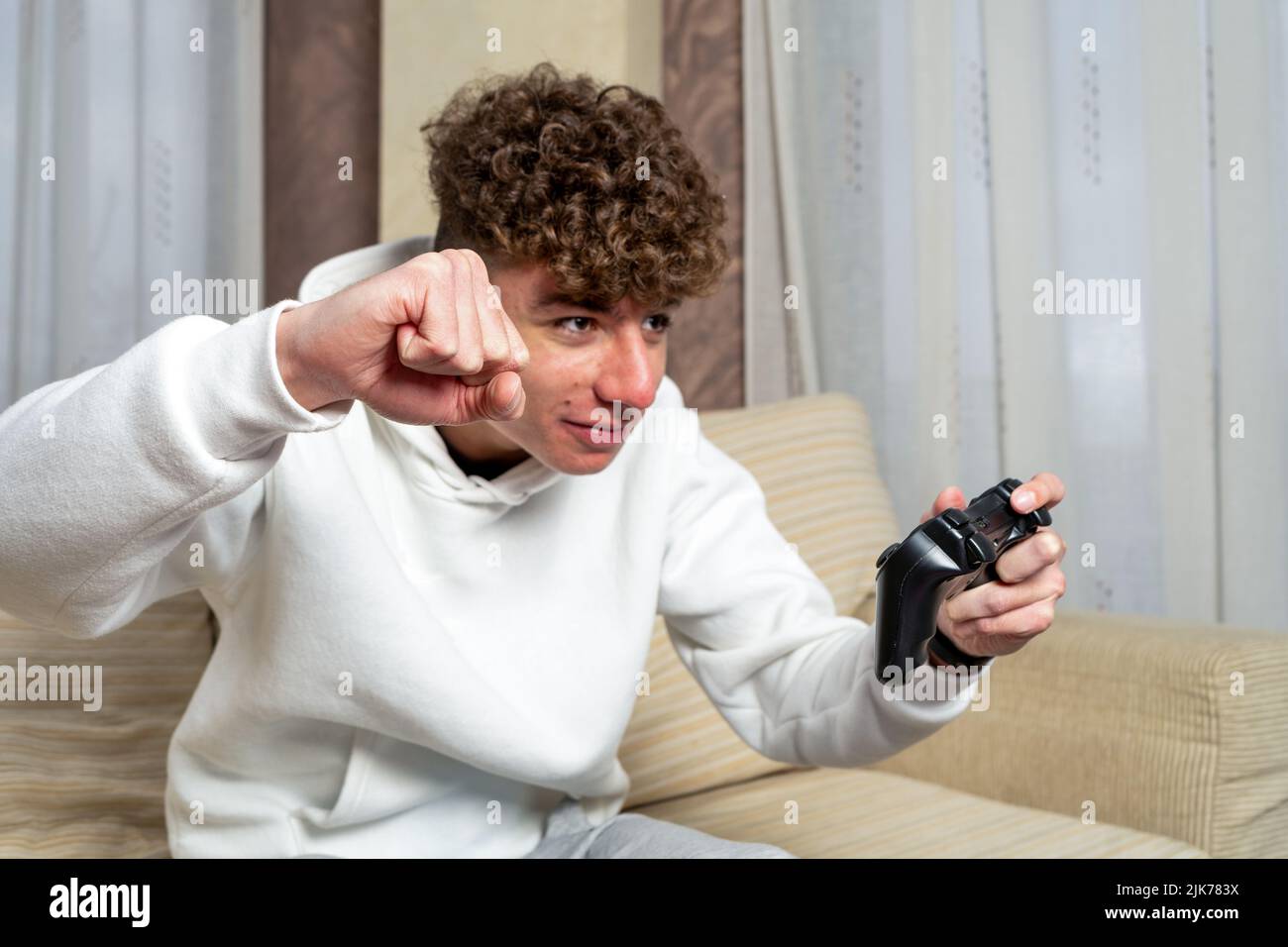 Frustrated young man playing video games sitting at sofa and holding ...