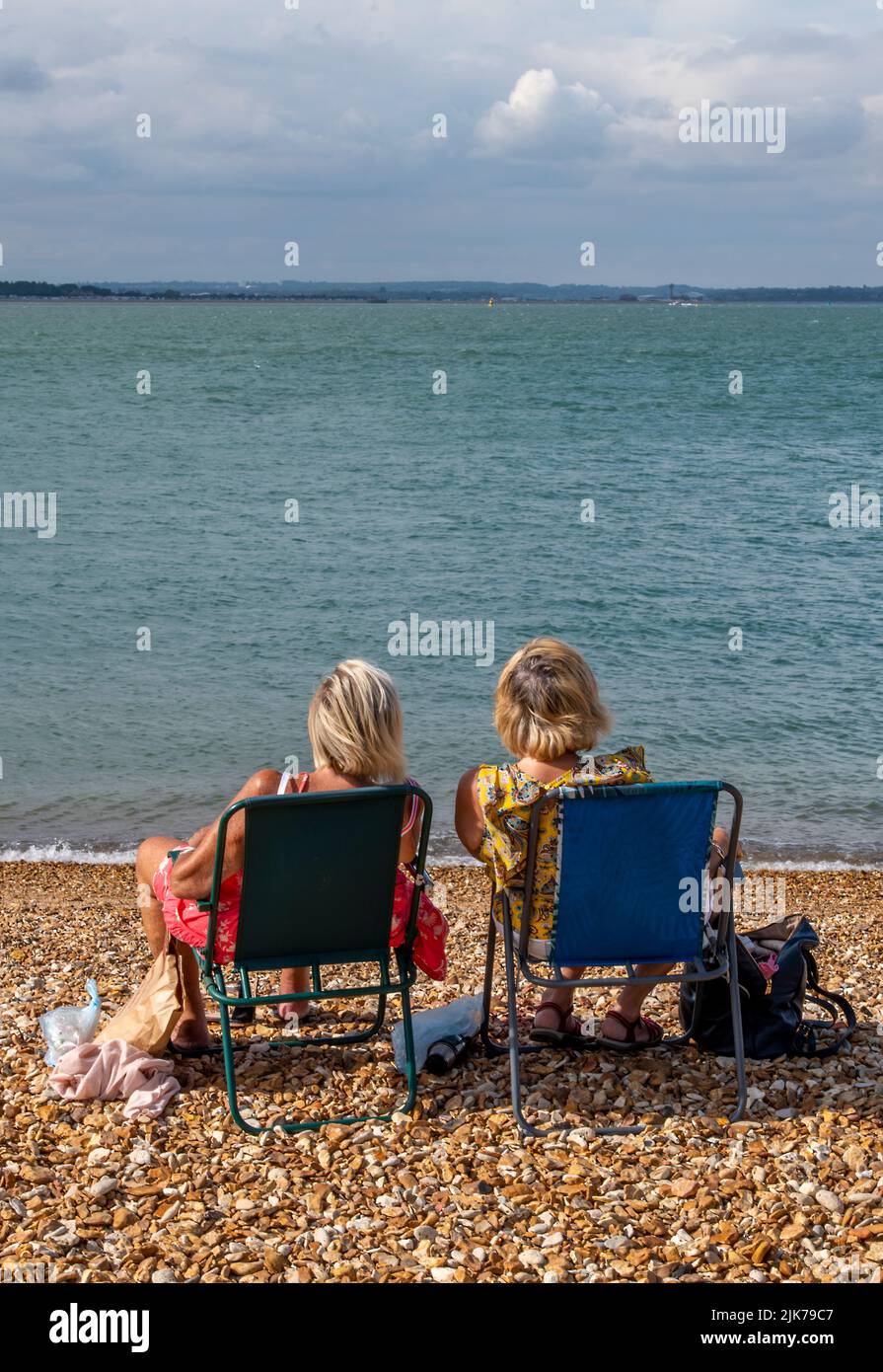 two older ladies sitting on a beach in chairs talking, two retired ...