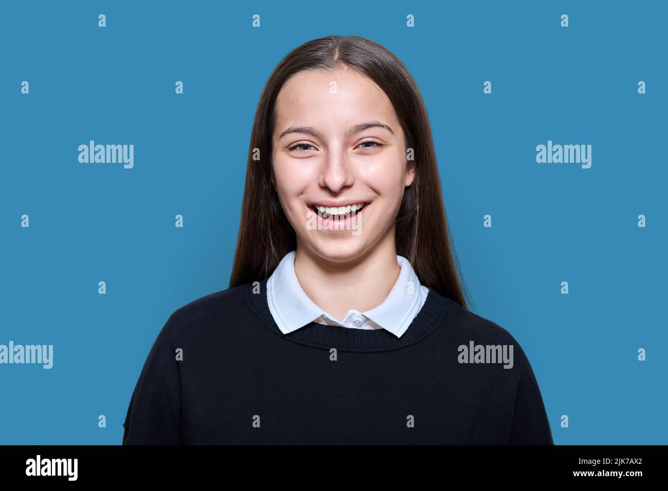 Portrait of teenage girl smiling looking at camera on blue color ...