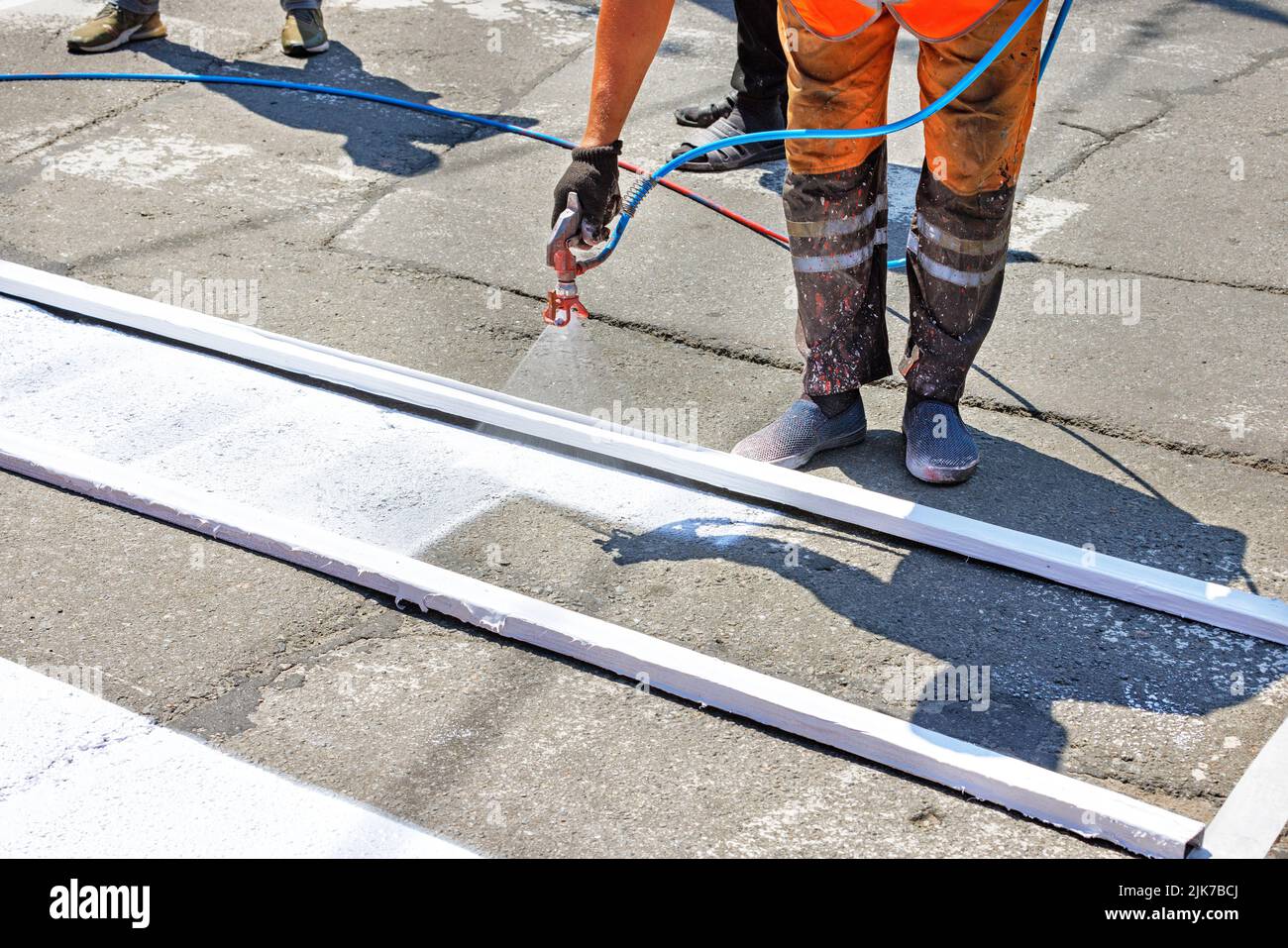 A road worker paints a white road marking of a pedestrian crossing ...