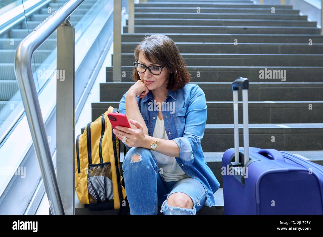 Woman passenger with suitcase backpack sitting on steps in modern ...