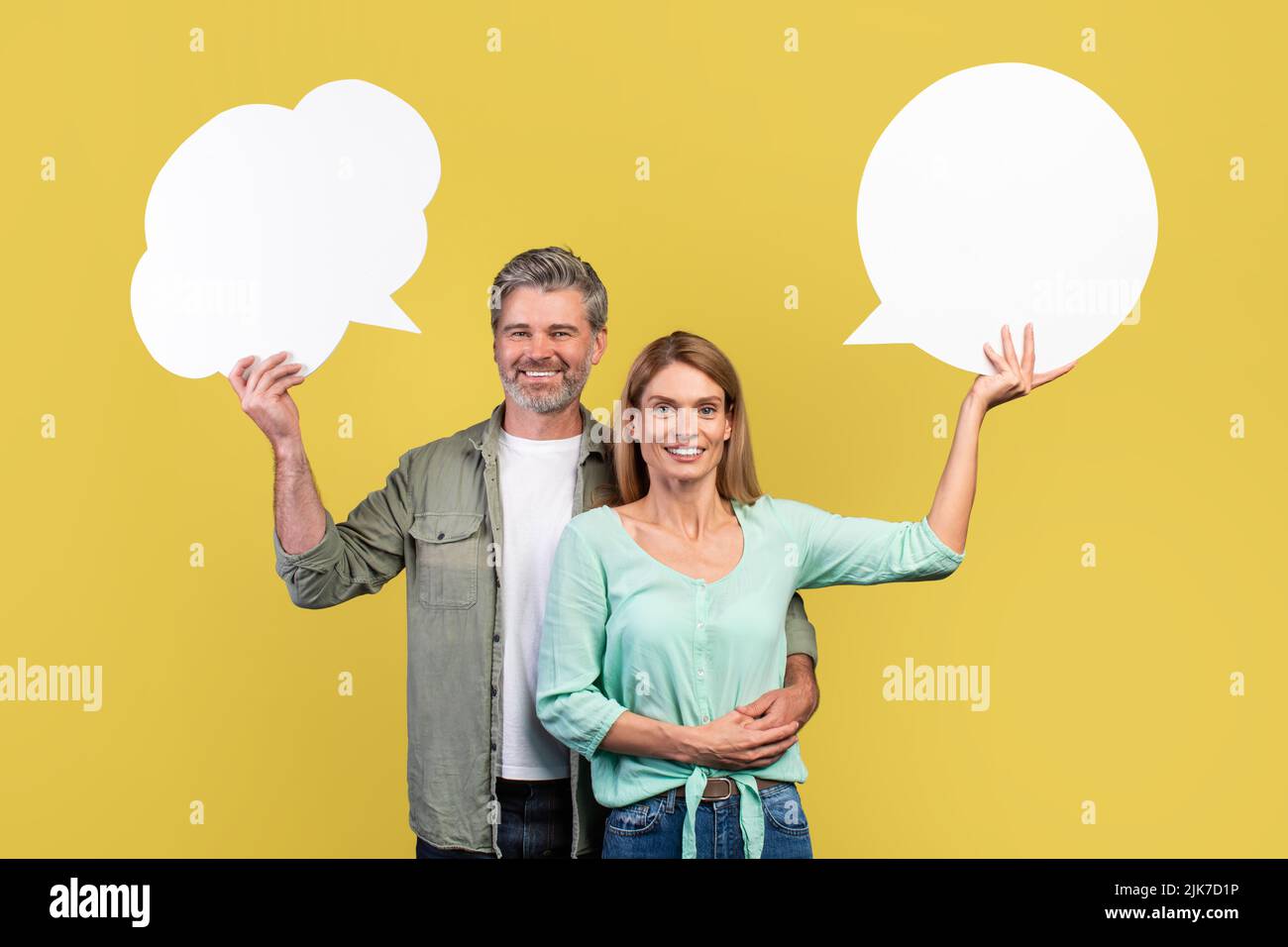 Happy middle aged spouses holding empty speech bubbles on yellow studio ...
