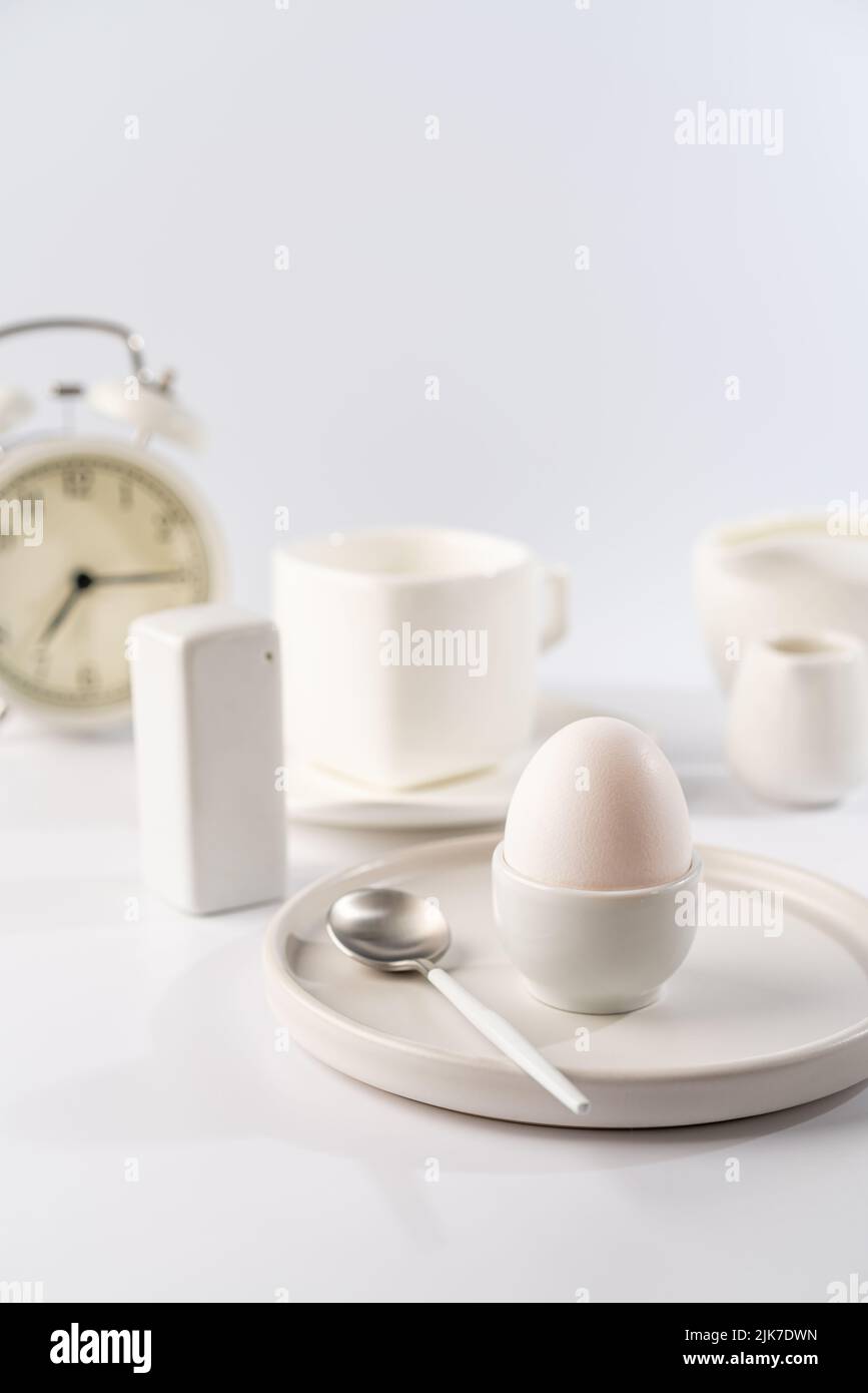 White egg with white plates, cup and alarm clock over white background ...