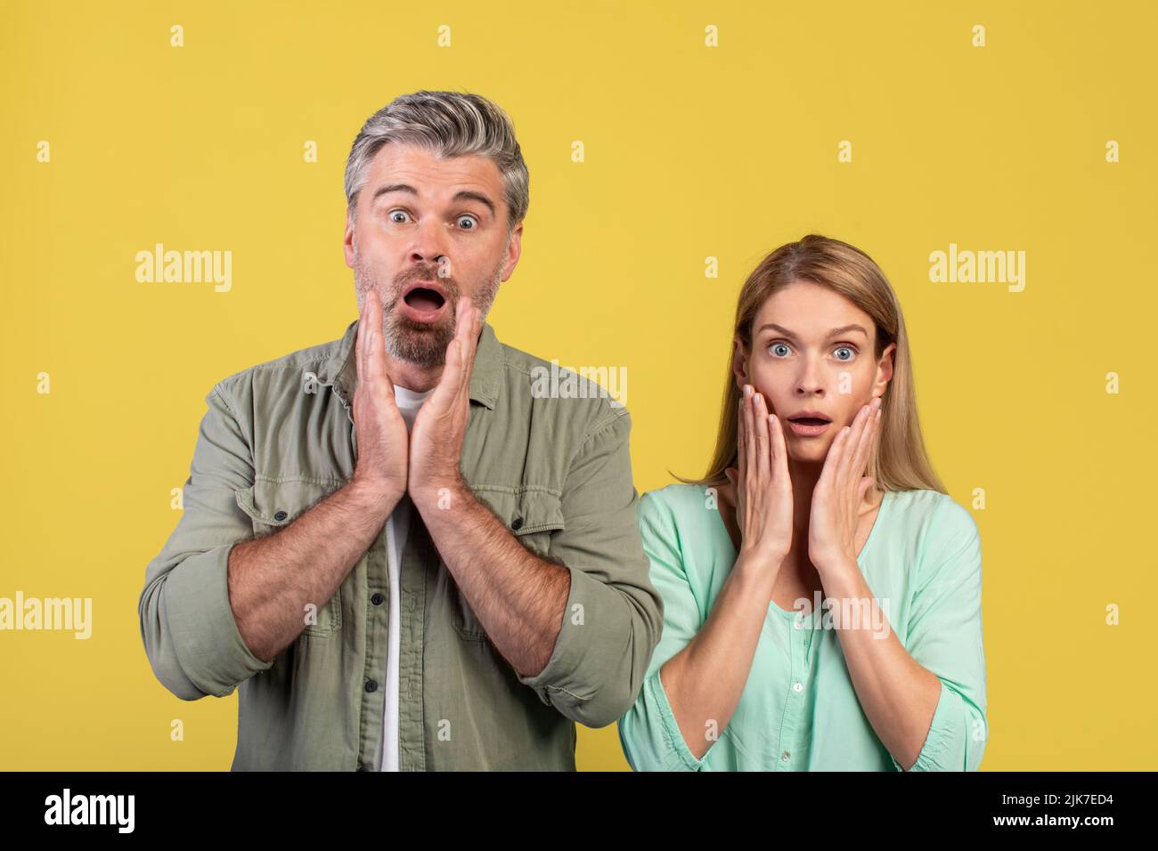 Omg. Shocked middle aged spouses touching face and cheeks, looking at ...