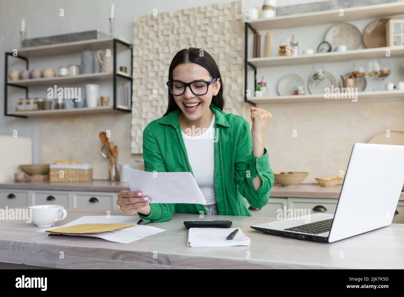 Happy woman in glasses and green shirt at home doing paper work got ...