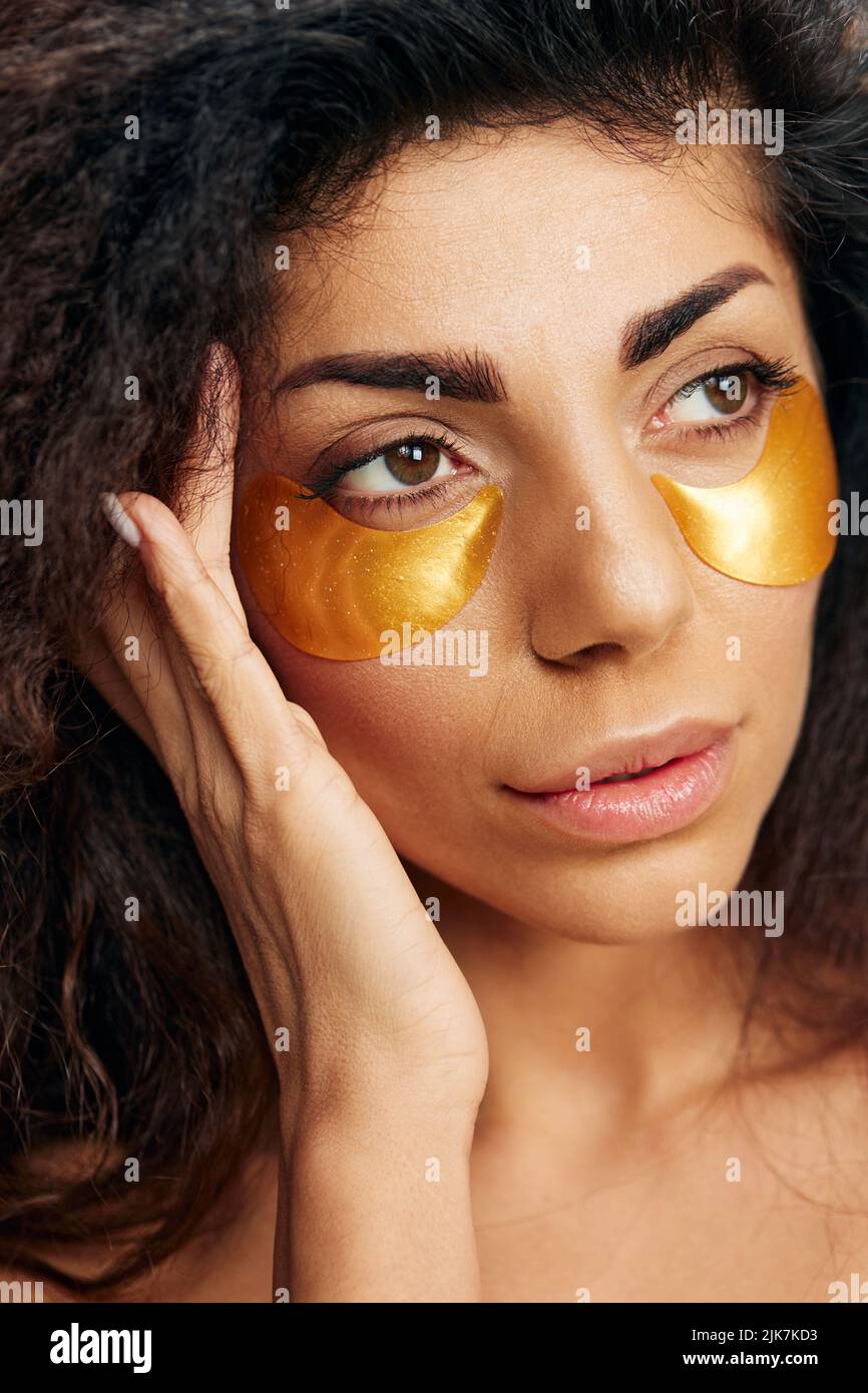 Pensive attractive Latin lady with gold hydrogel patches under eye ...