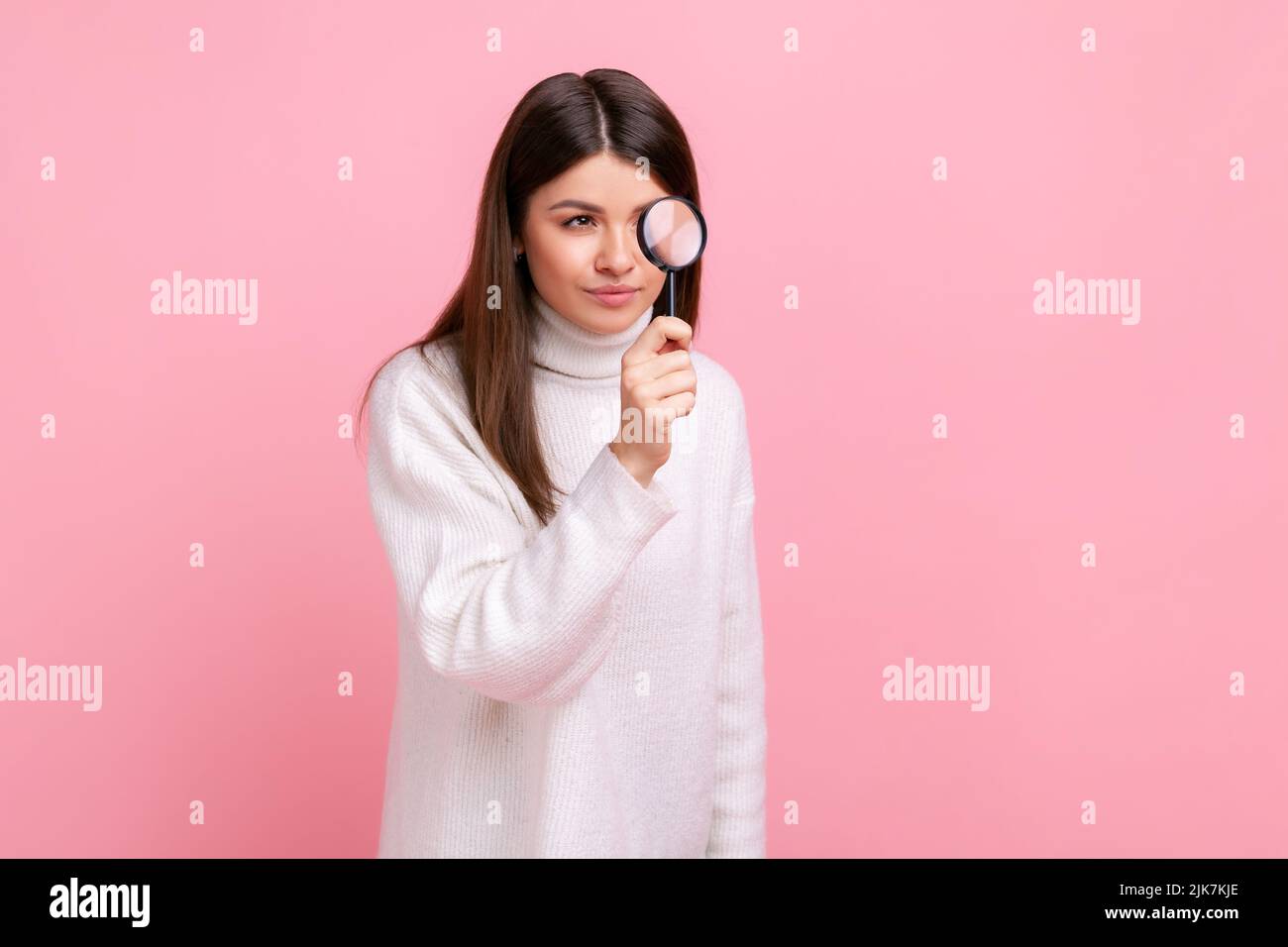 Curious female looking away through magnifying glass, finding out ...