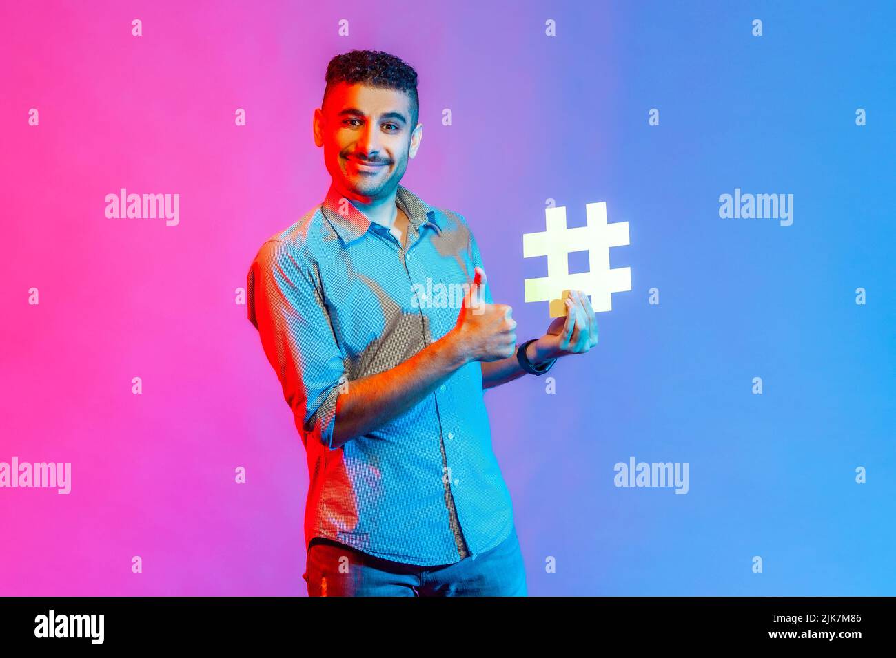 Portrait of smiling man in shirt holding hashtag symbol, showing thumb ...