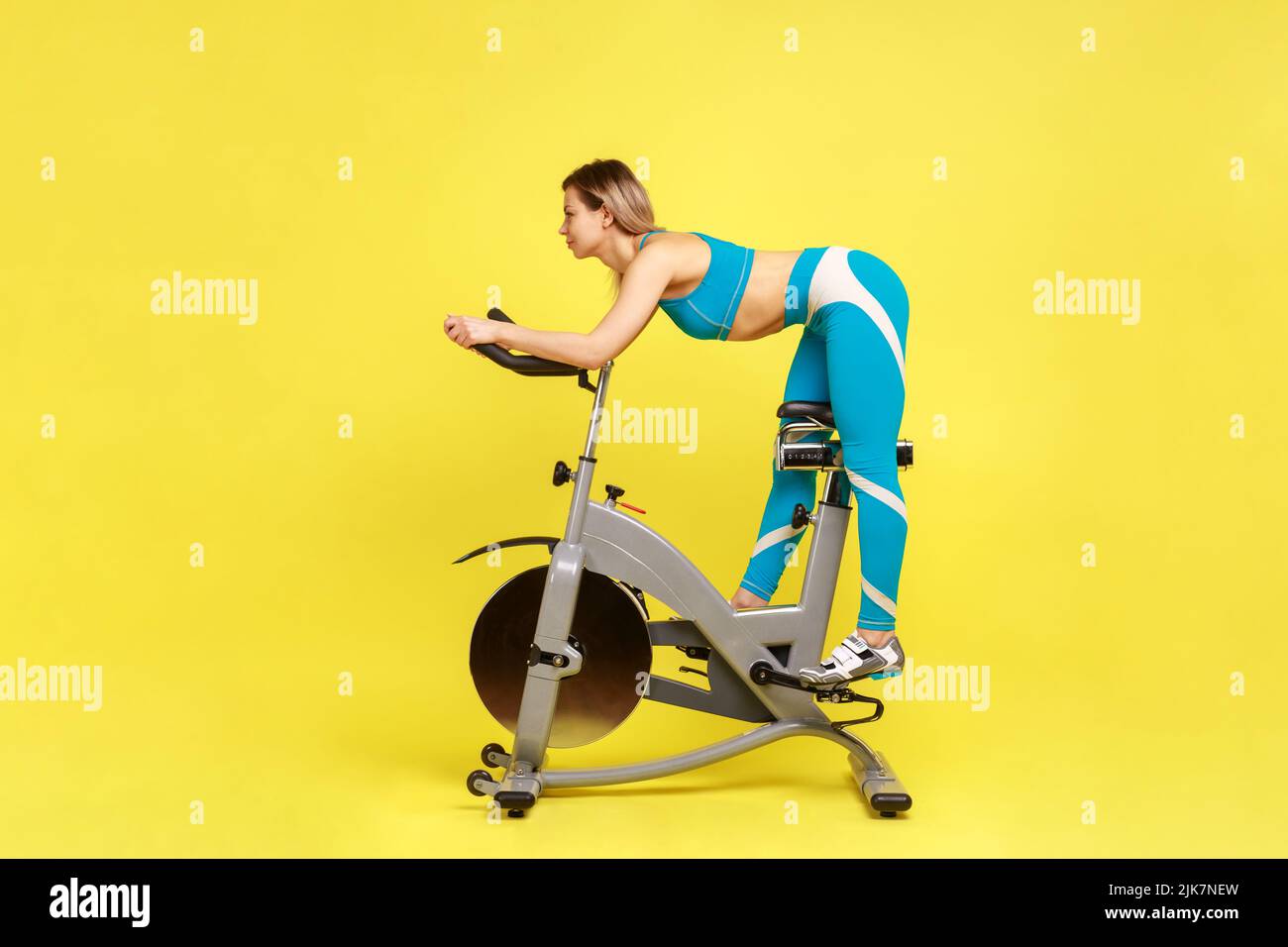 Side view of slim attractive sporty woman on exercise bike, looking ...