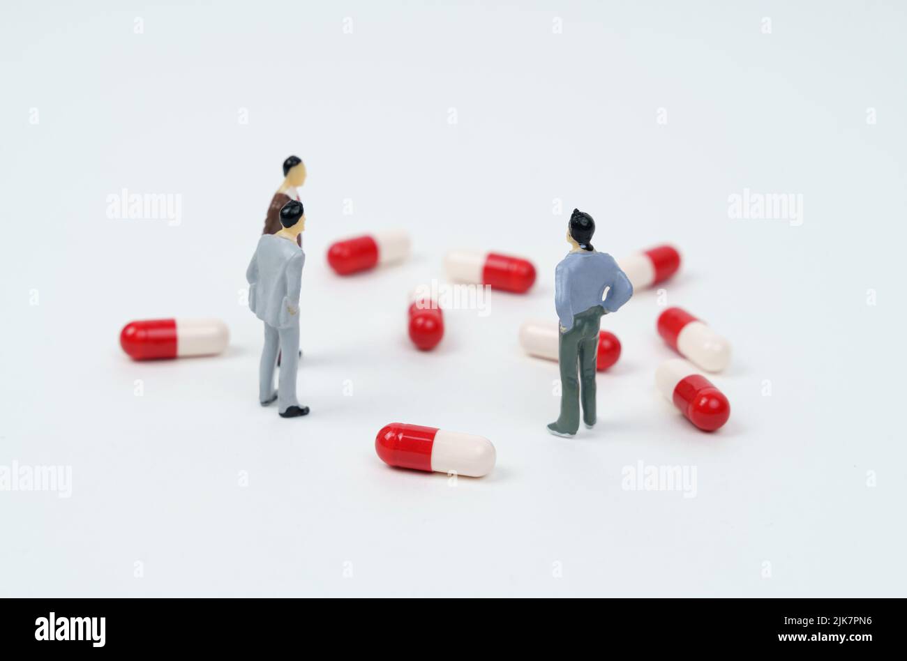 Three miniature figurines of people stand among medical capsules. The ...