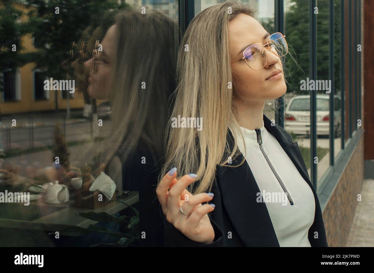 A beautiful woman stands leaning against the window of a building ...