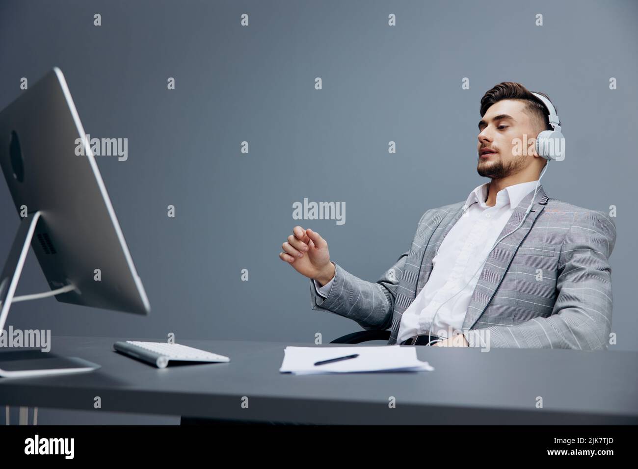 handsome man in headphones in a gray suit sits in front of a computer ...