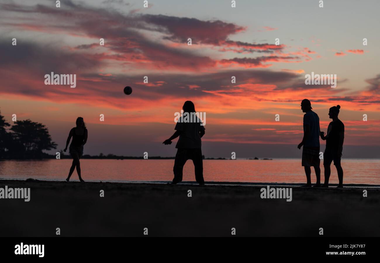 Sunset beach soccer. People in silhouette play football on the beach as ...