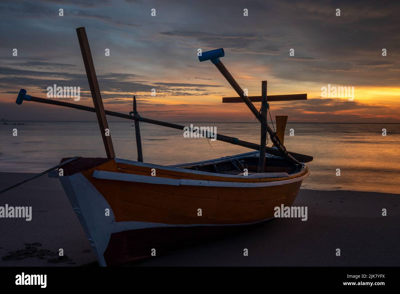 A wooden boat with wooden cross and oars, on a sandy beach by the sea ...