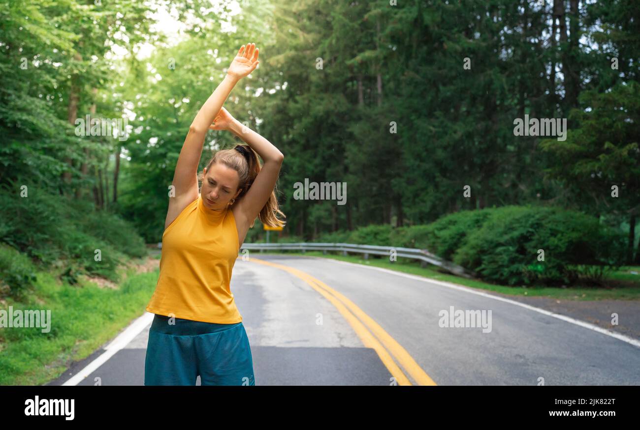 Young fitness woman runner with stretching before run in road in nature. Healthy lifestyle and ...