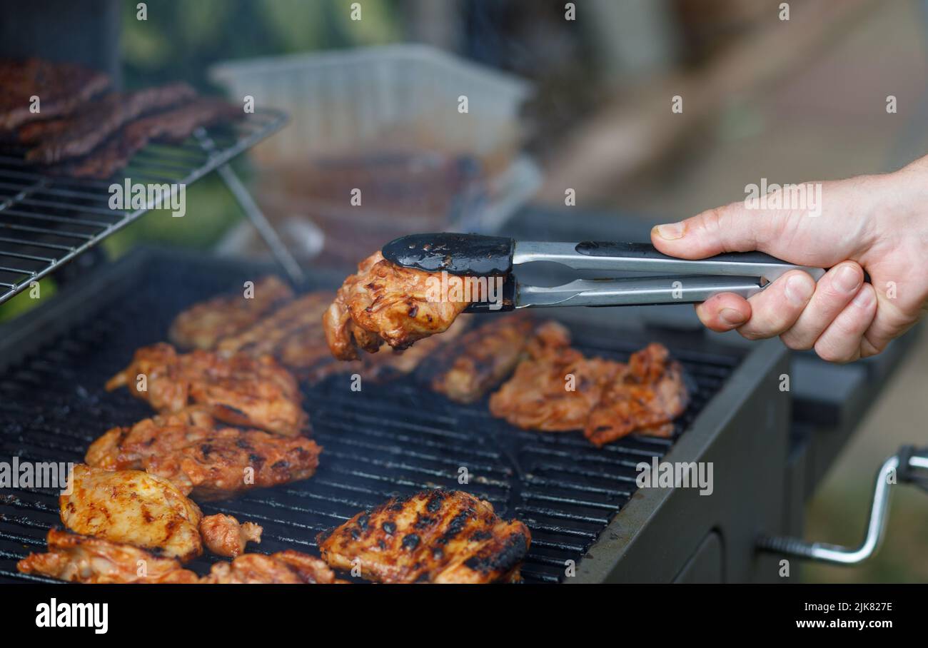 Male hand holding tongs with barbecue chicken on a metal bbq grill ...