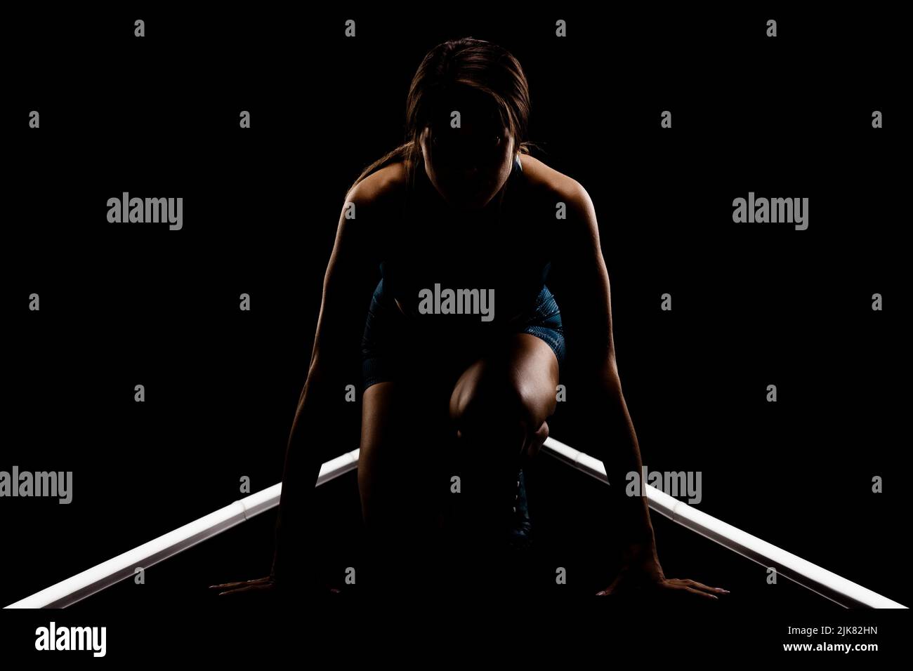 Female runner in race start position. Girl in sportswear posing on lit ...