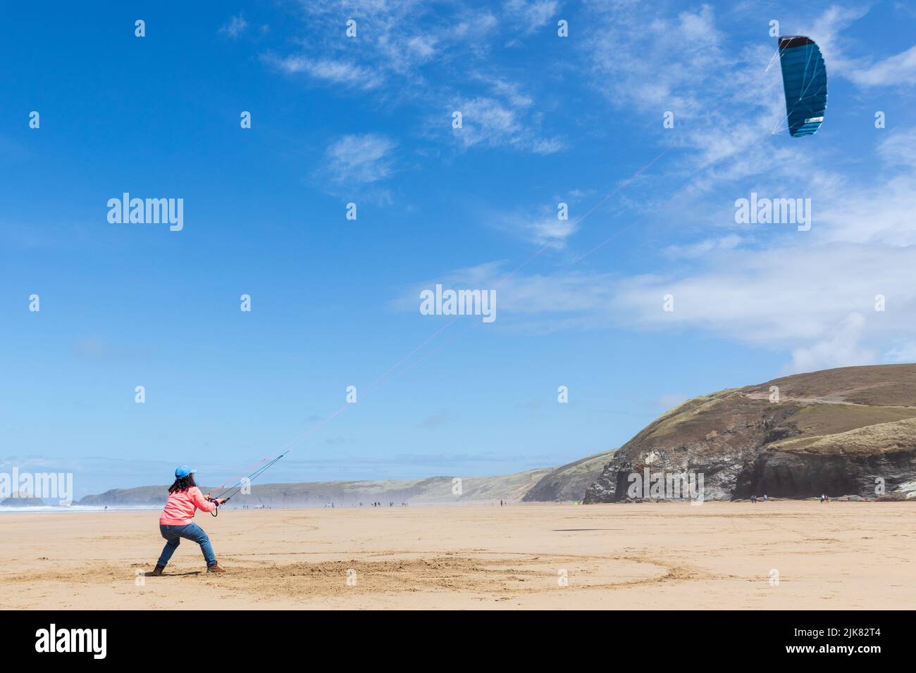 A lady flies a power kite on the beach with the kite soaring through ...