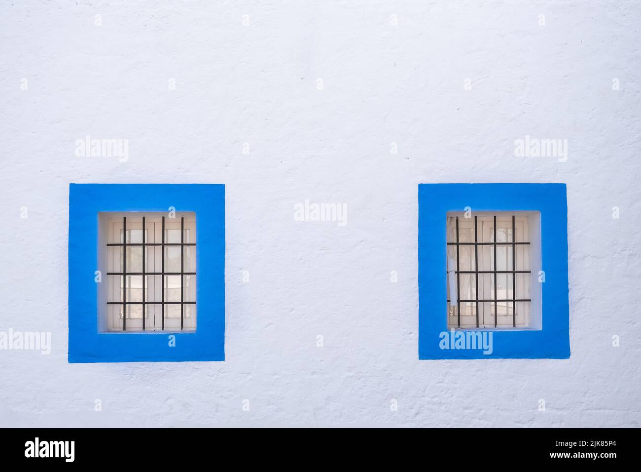 two windows with blue frames on the whitewashed facade of a house ...